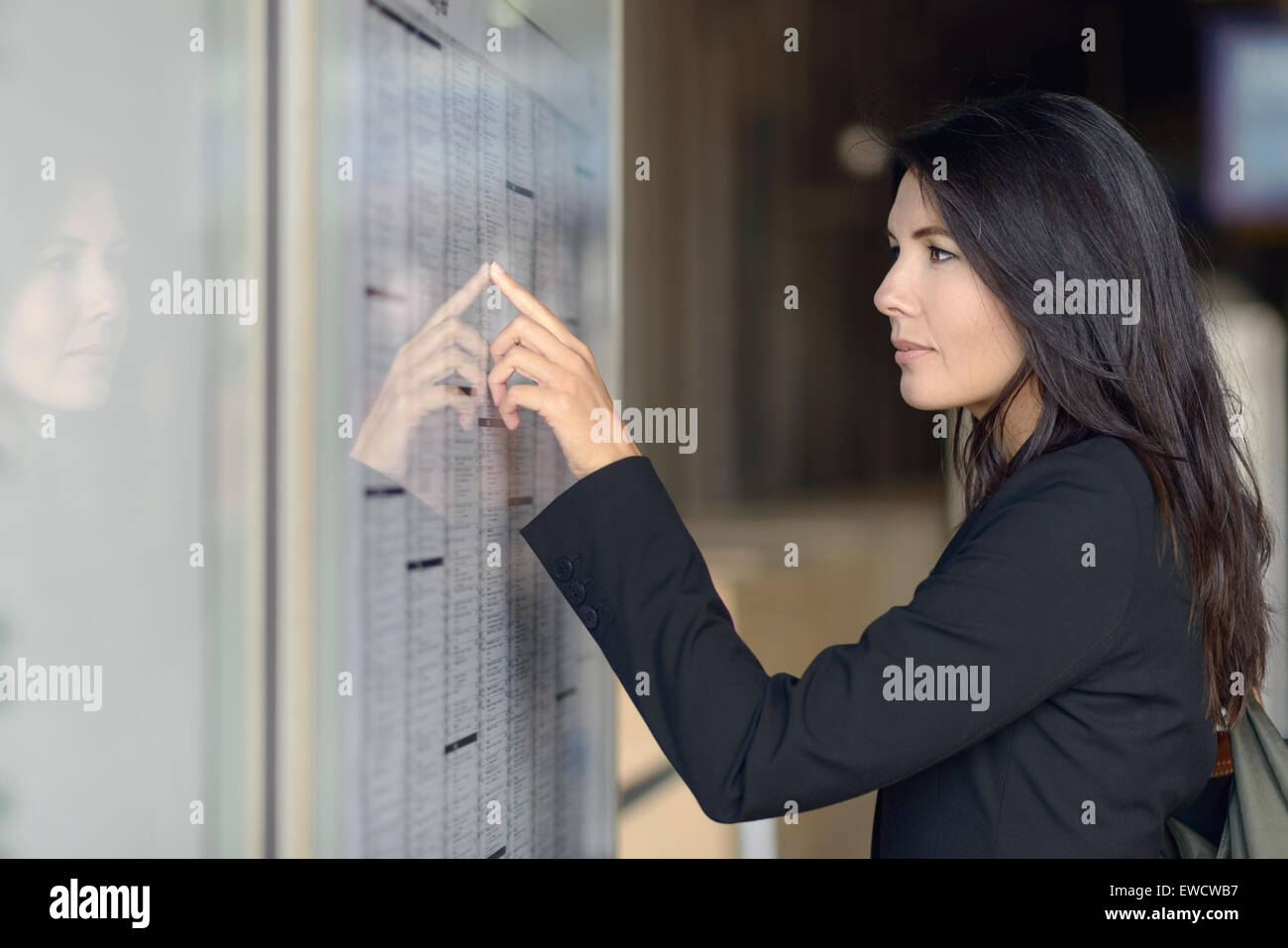 Attractive woman reading the train timetable running down the columns ...