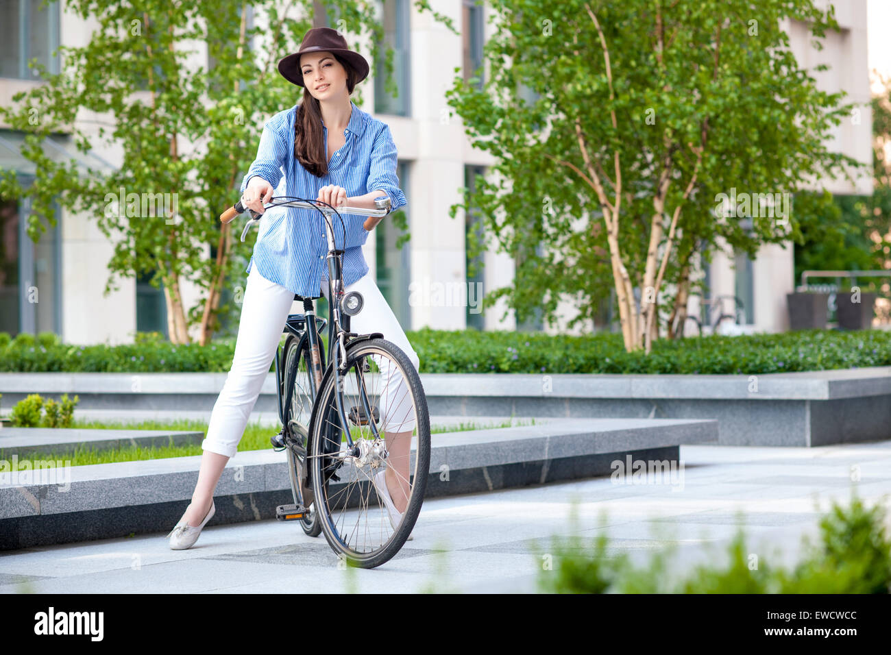 Pretty smiling girl in hat and blue dress riding a bicycle at green ...