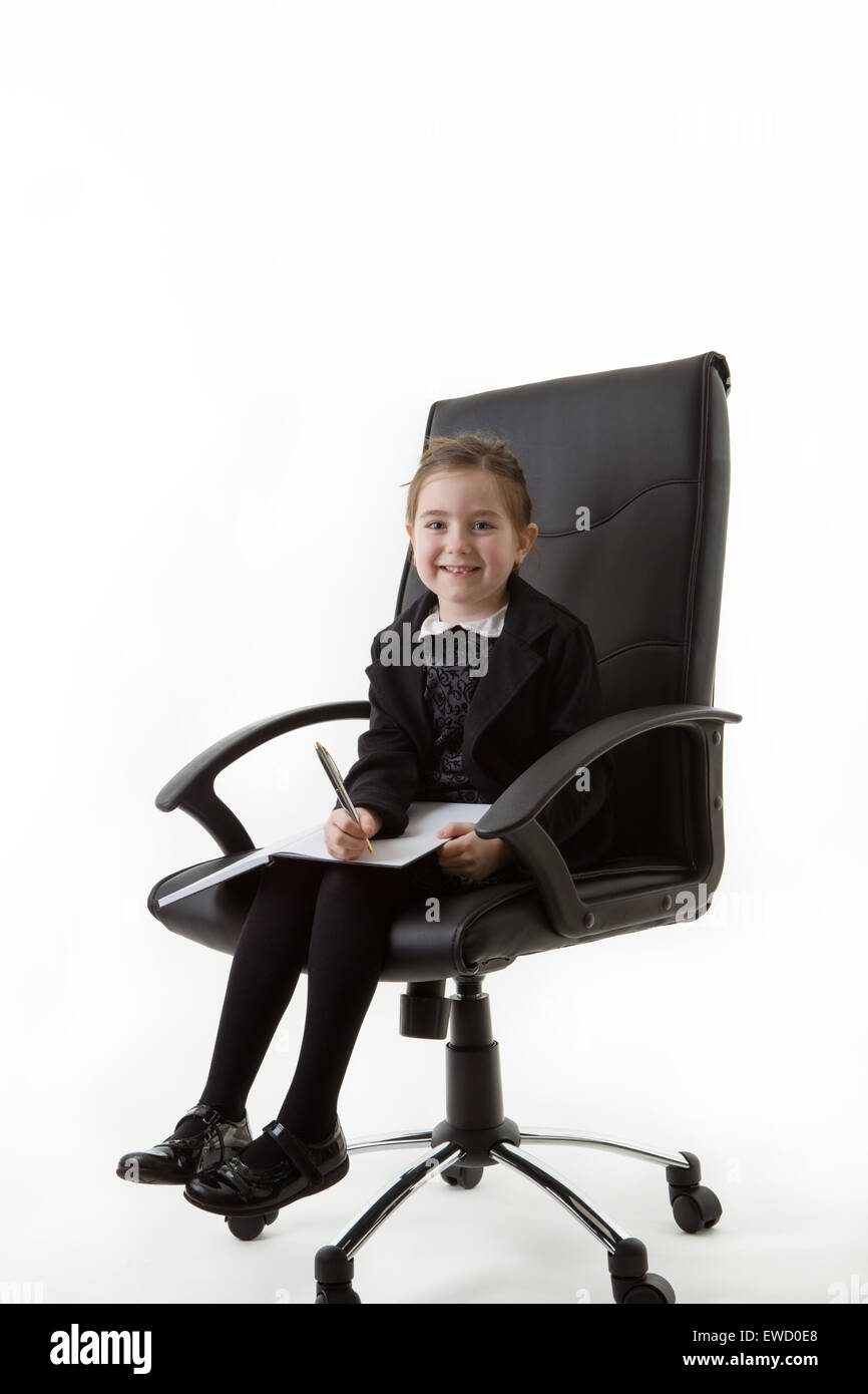 young girl siting in a office chair writing something in a note book ...