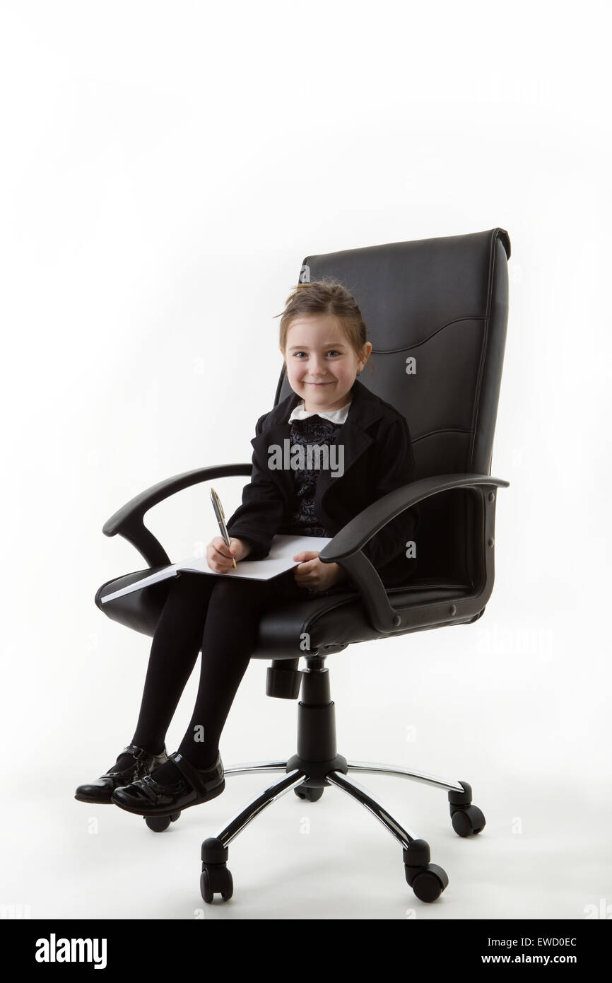 young girl siting in a office chair writing something in a note book ...