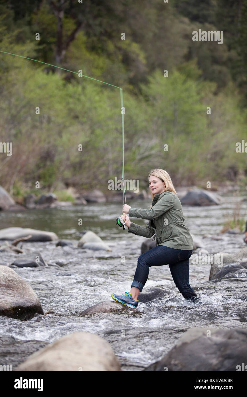 A young, adventurous woman fly fishing in the fast moving current of ...