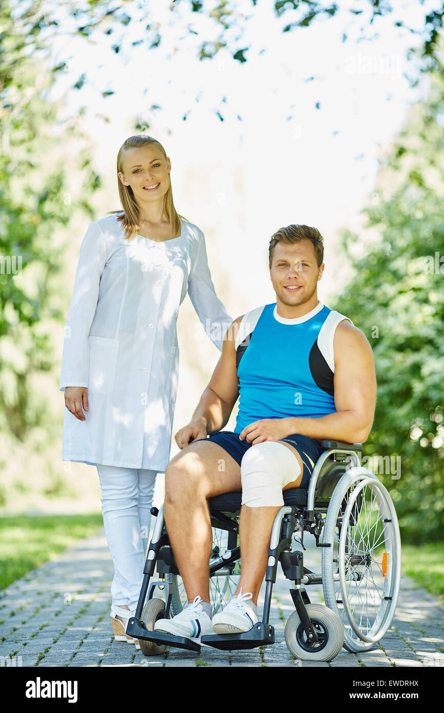 Pretty caregiver walking with male patient in a wheelchair in park ...