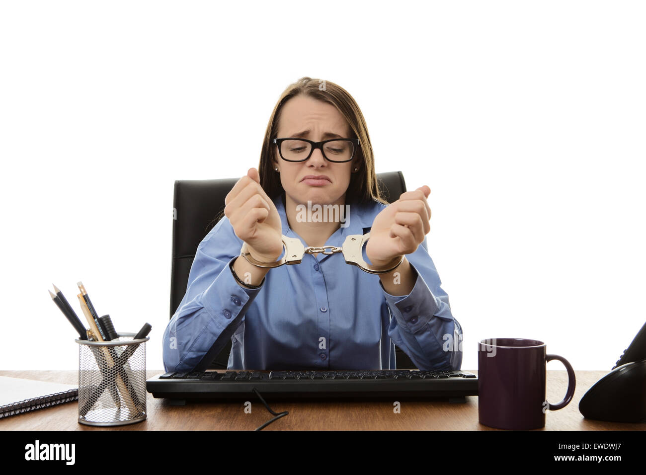 woman sitting at her desk at work with her hands handcuffed together ...