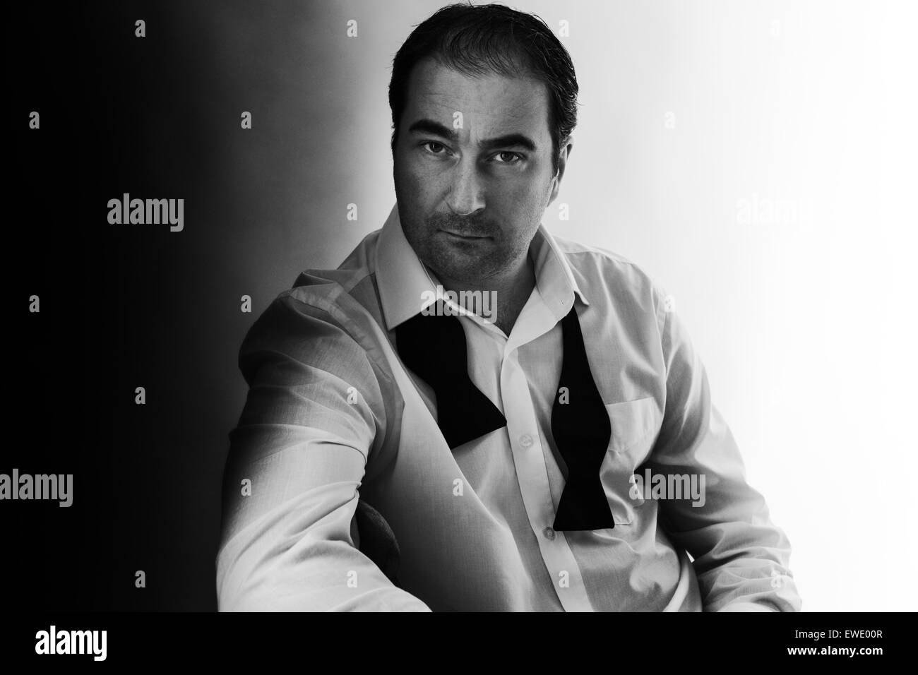 guy siting on a chair with a bow tie undone around his neck Stock Photo ...