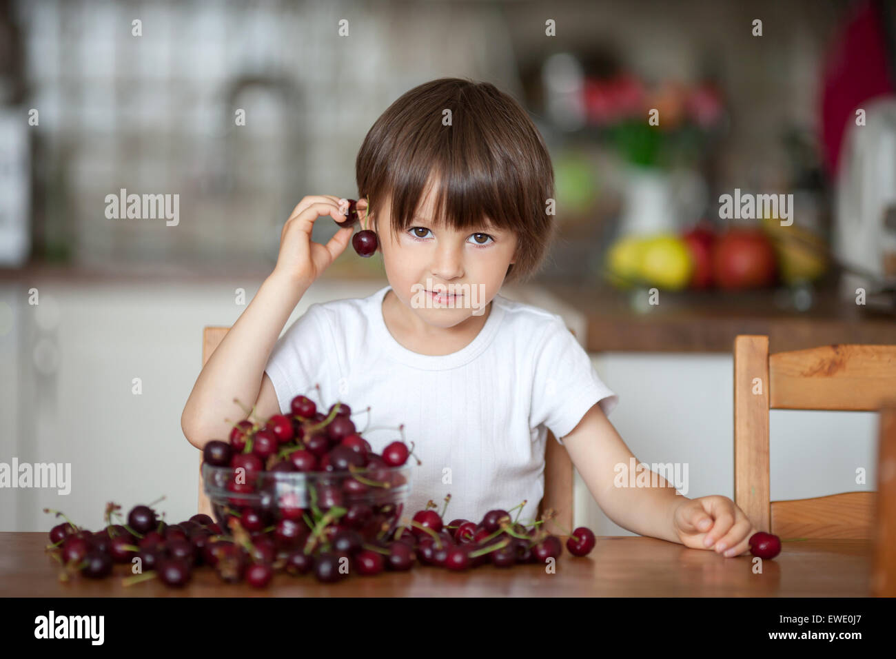 Cute little boy, eating cherries at home in the kitchen, making funny ...