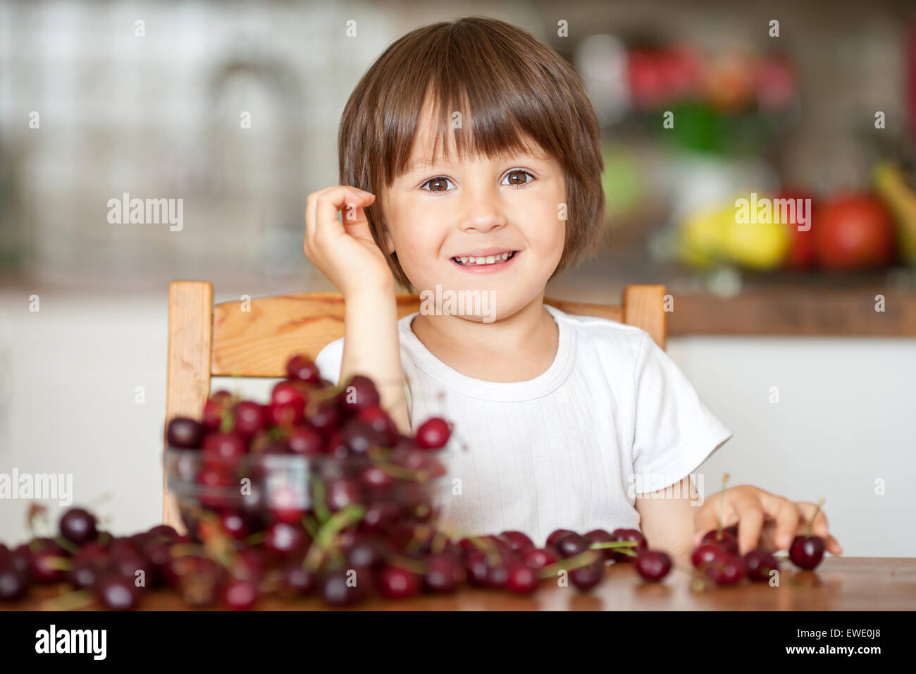 Cute little boy, eating cherries at home in the kitchen, making funny ...