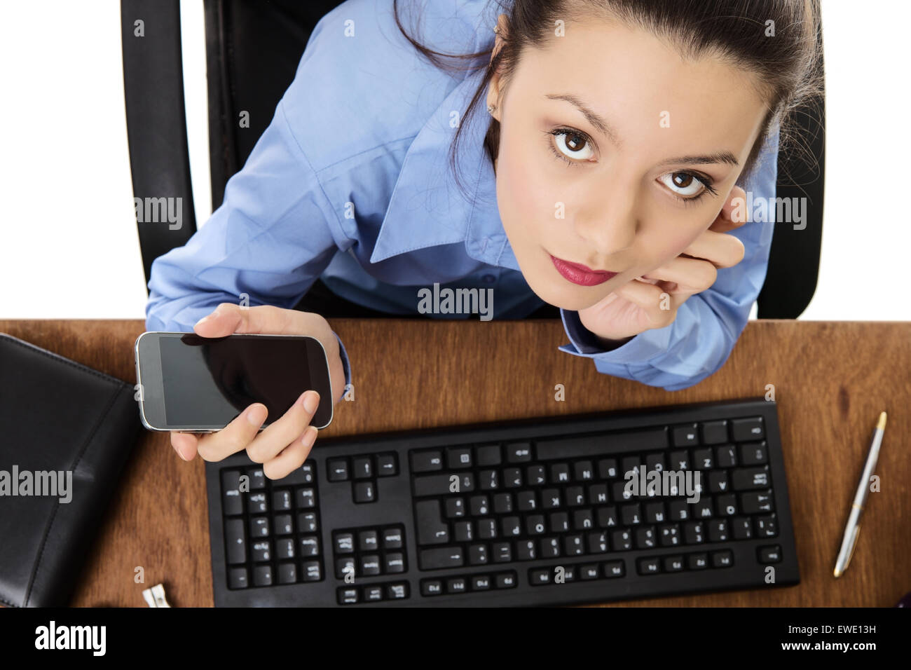 woman at hers desk looking up holding a mobile phone shot from a birds ...