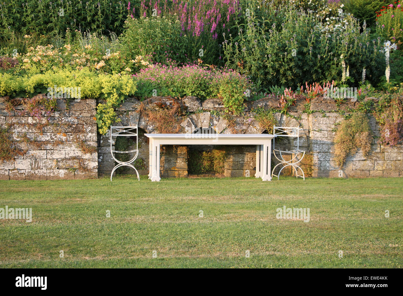 An off-white wooden table on a lawn with herbaceous border behind and ...
