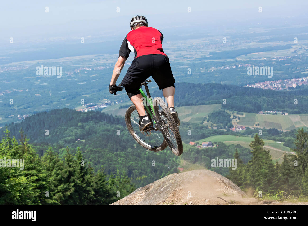 Rear view of mountain bike rider who jumps over a dirt track kicker ...