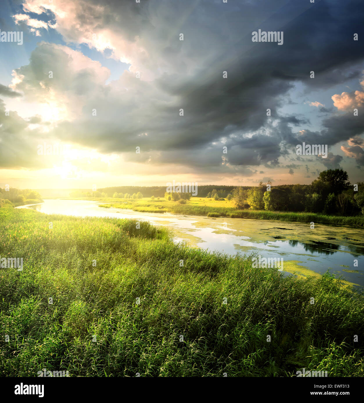River flows through the field with lush green grass under a dramatic ...