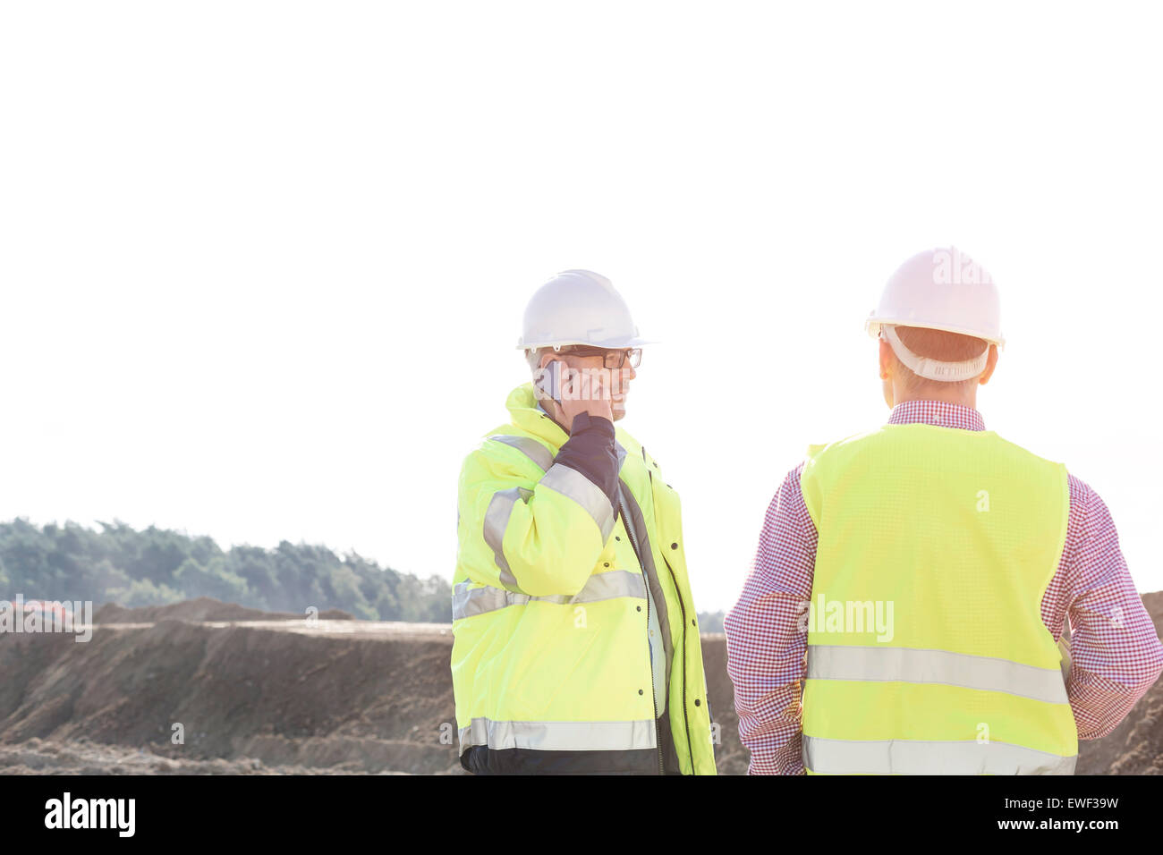 Male engineer using mobile phone while standing with colleague at ...