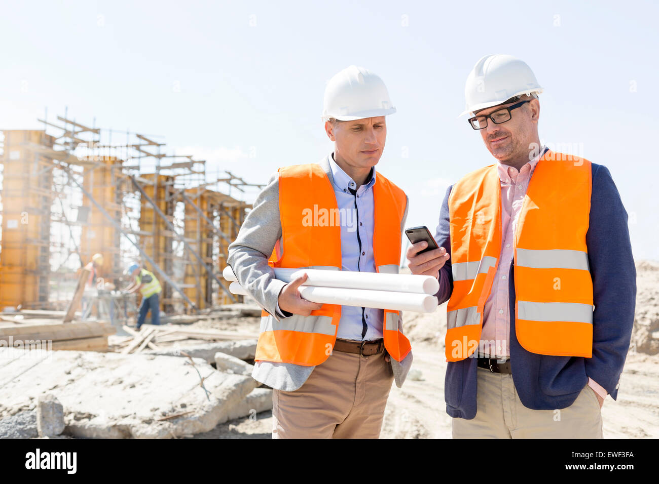 Male engineers using mobile phone at construction site against clear ...