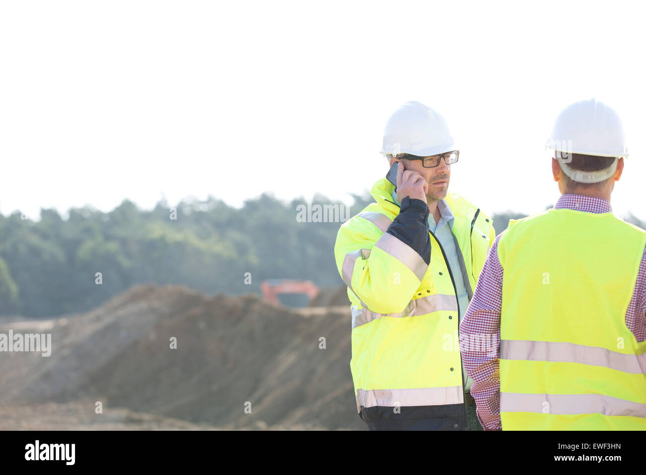 Supervisor using mobile phone while standing with colleague at ...