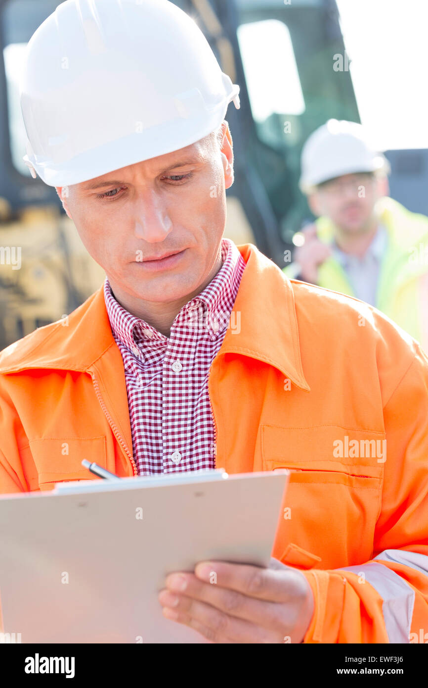 Supervisor writing on clipboard at construction site with colleague in ...