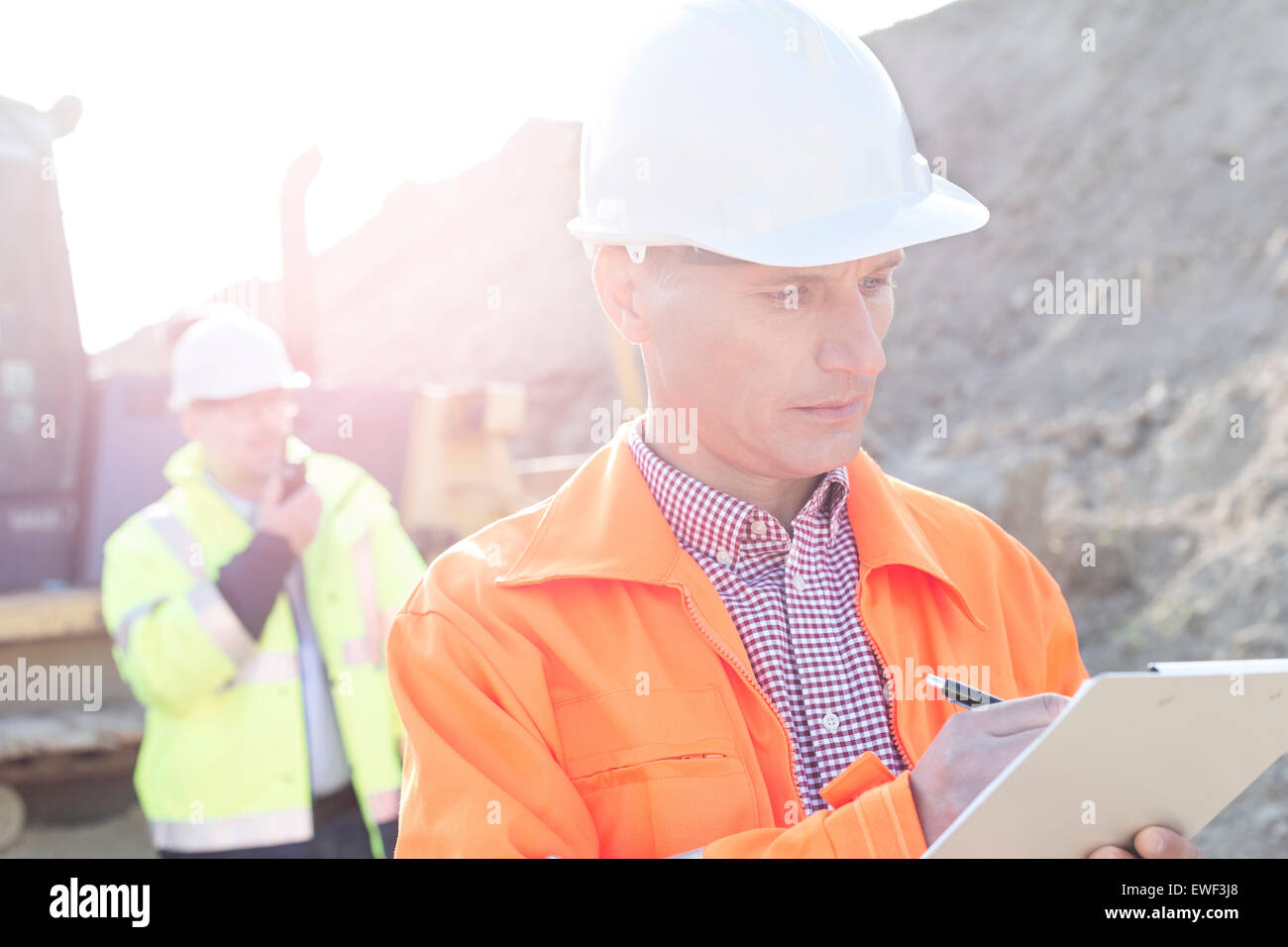 Engineer writing on clipboard at construction site with colleague in ...