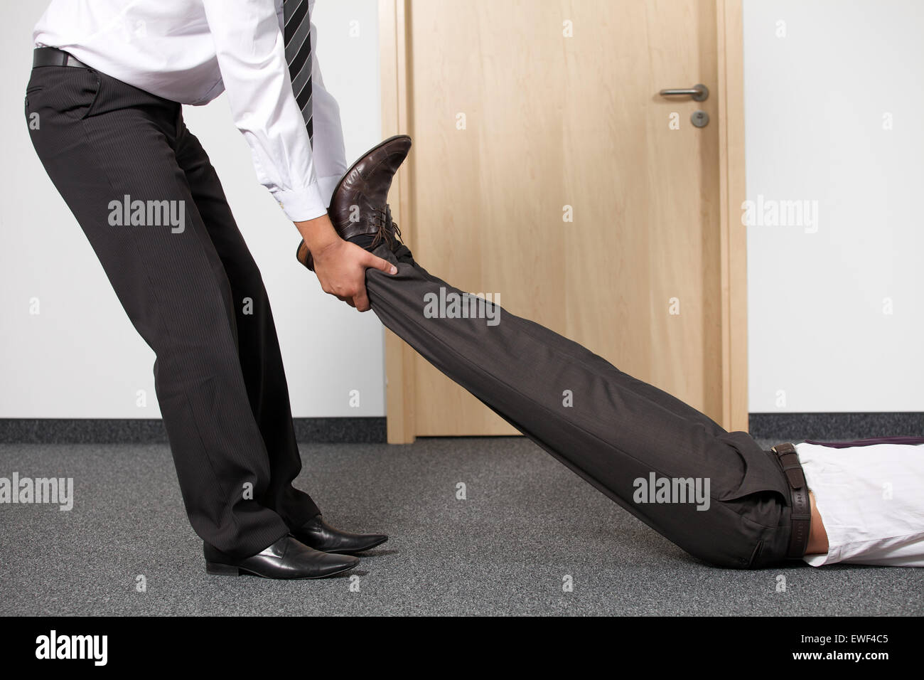 Businessmen pulling colleague's leg at office Stock Photo - Alamy