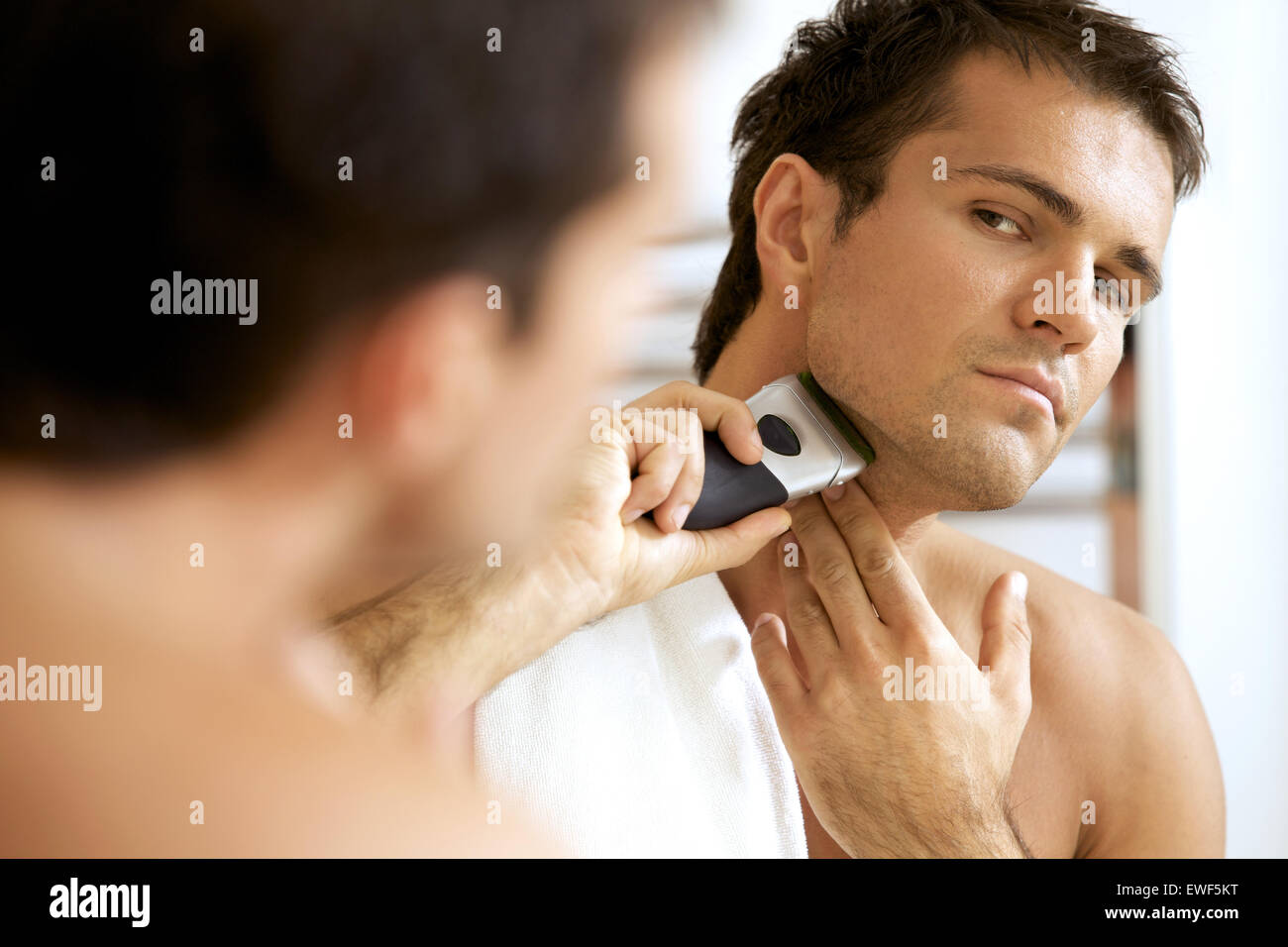 Reflection of young man in mirror shaving with electric shaver Stock ...