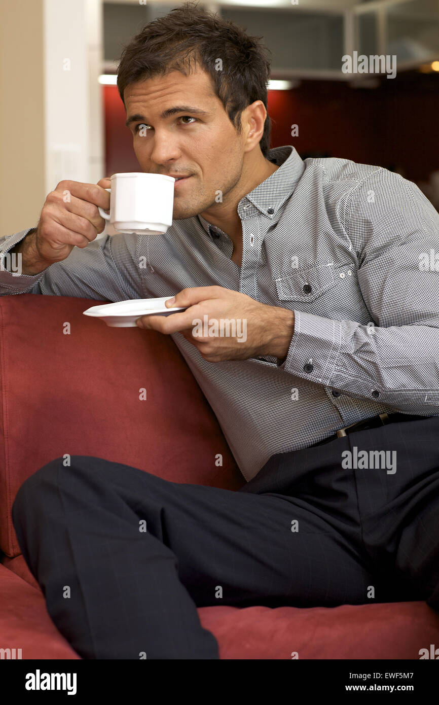 Young man drinking tea, sitting in sofa Stock Photo - Alamy