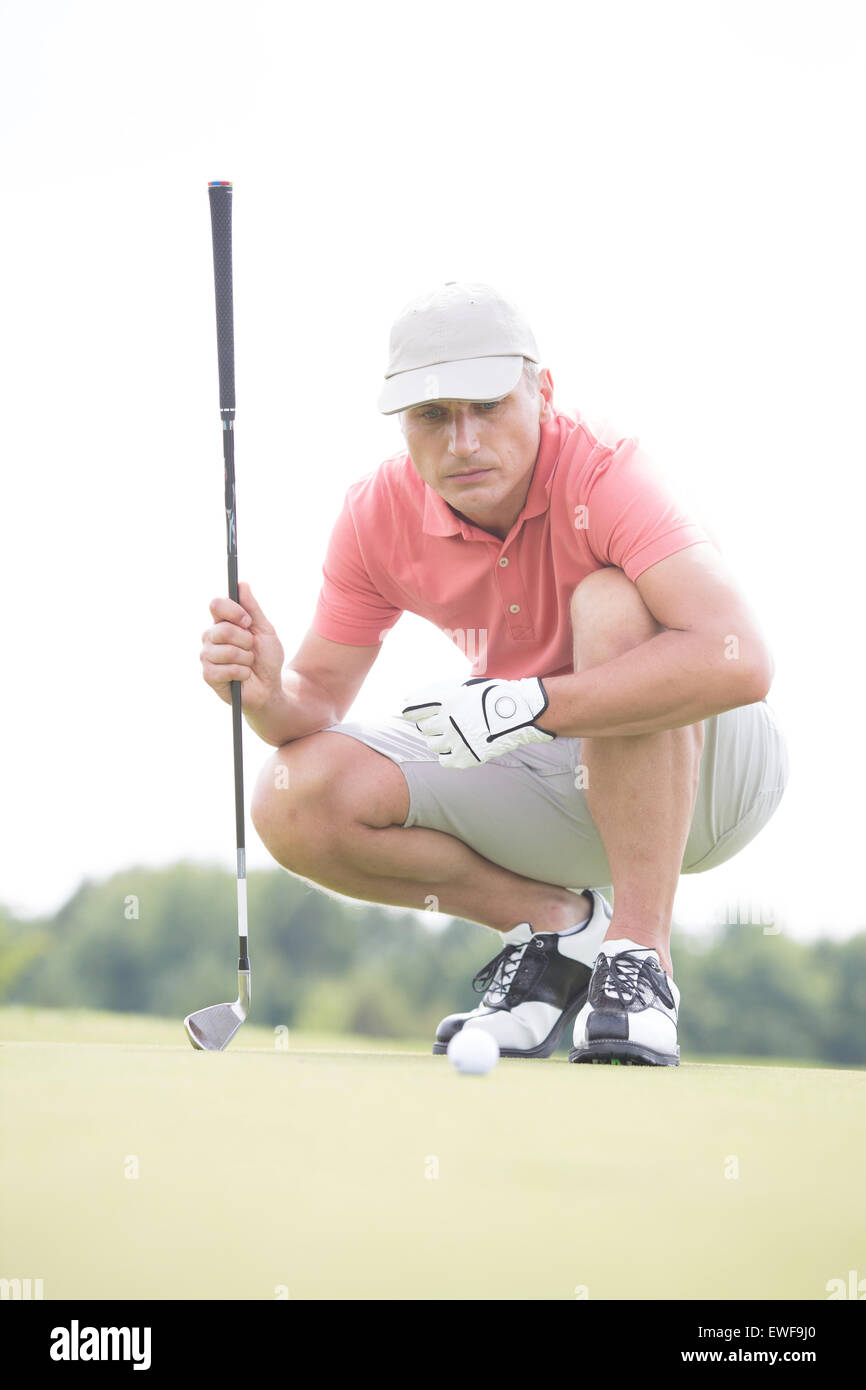 Middle-aged man aiming ball while crouching on golf course Stock Photo ...