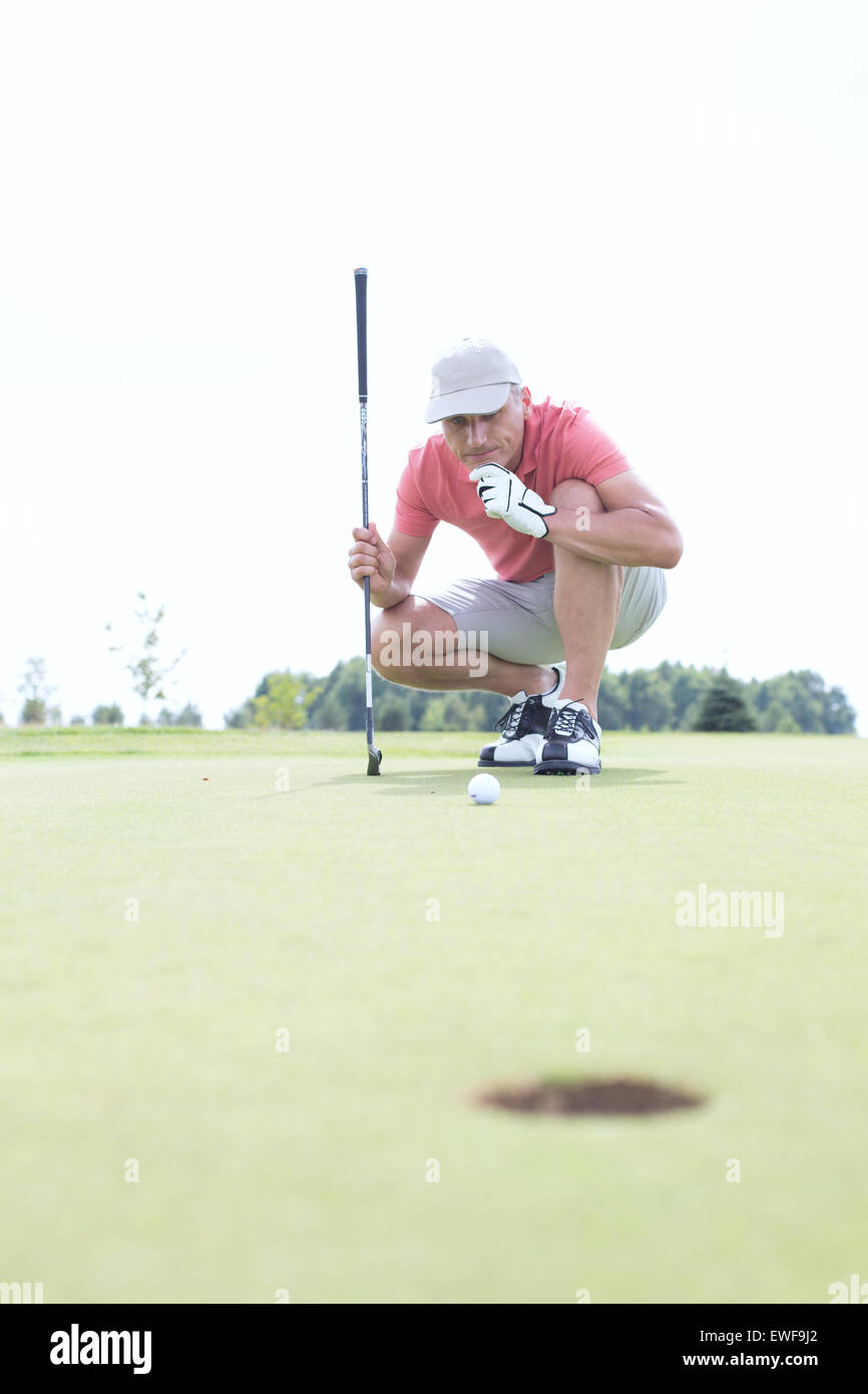 Middle-aged man looking at ball while crouching on golf course Stock ...