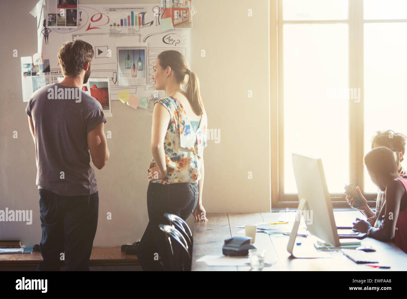 Creative business people reviewing proofs and notes on office wall ...
