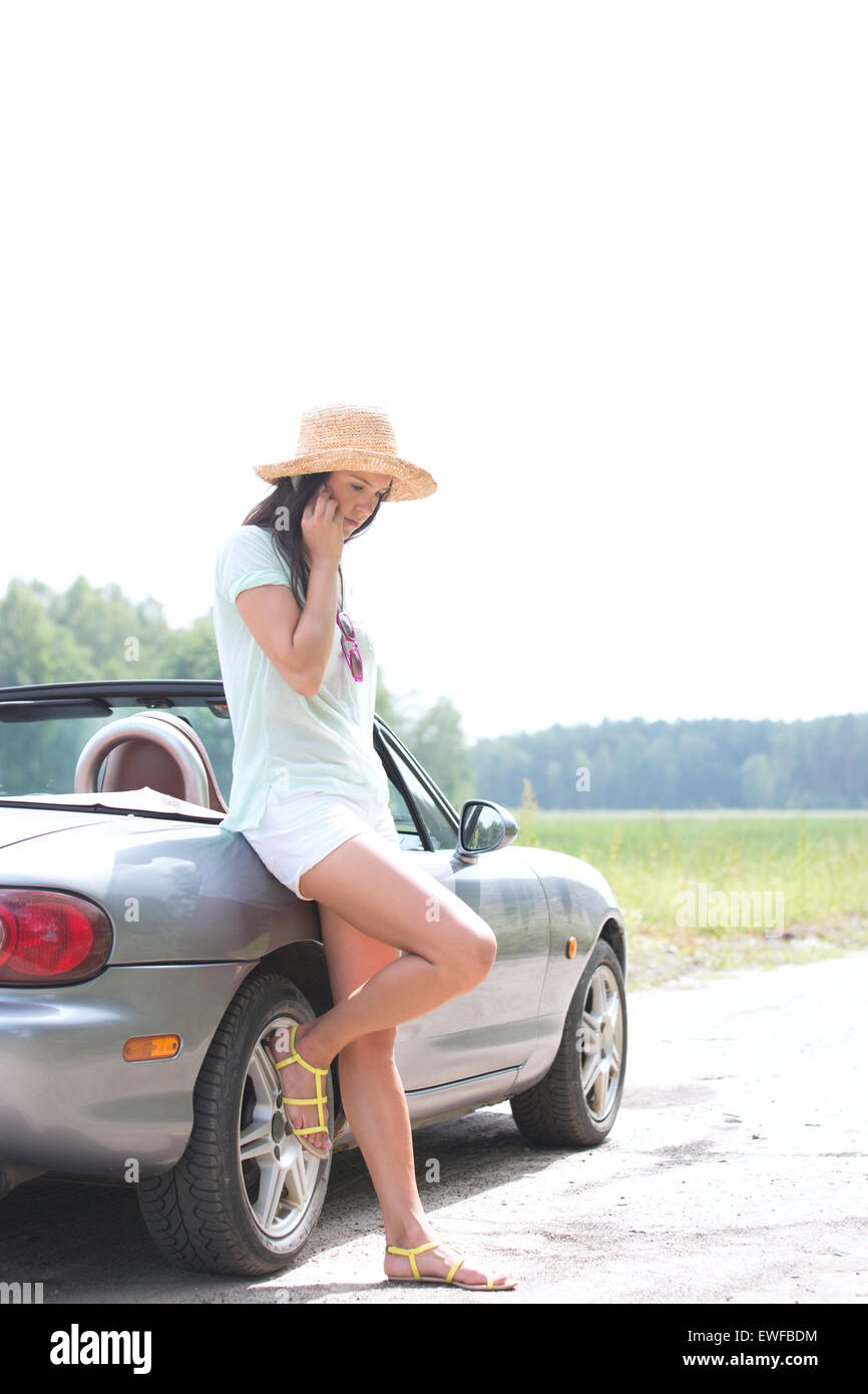 Full-length of woman using cell phone while leaning on convertible at ...