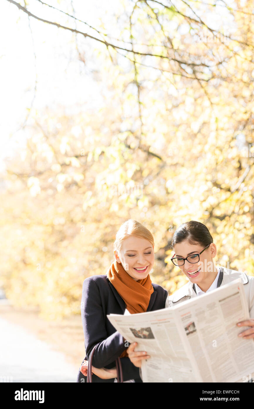 Happy businesswomen reading newspaper together at park Stock Photo - Alamy