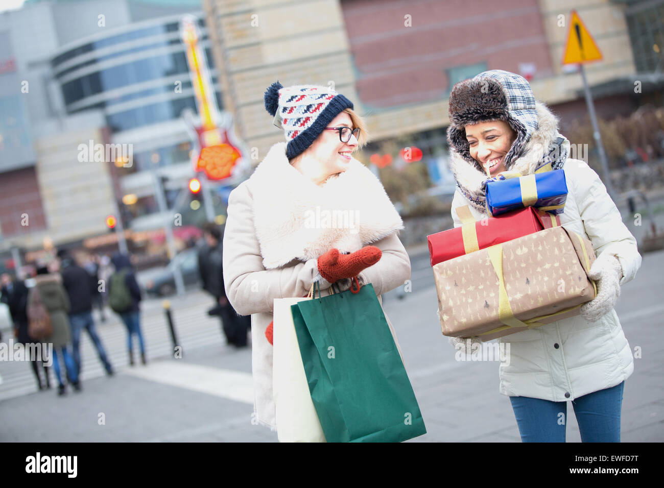Happy women with gifts and shopping bags walking on city street during ...