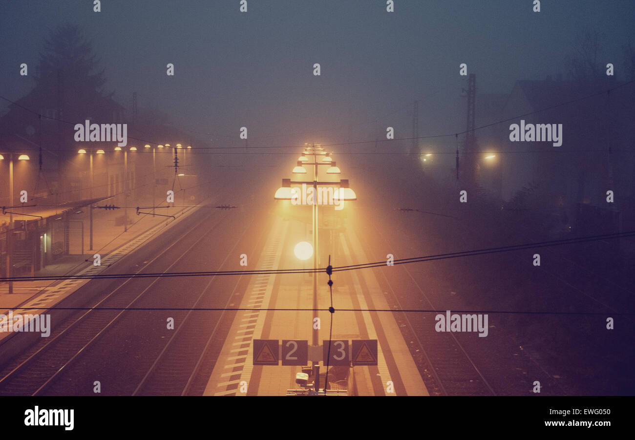 A train station is illuminated by soft lights, surrounded by thick fog ...