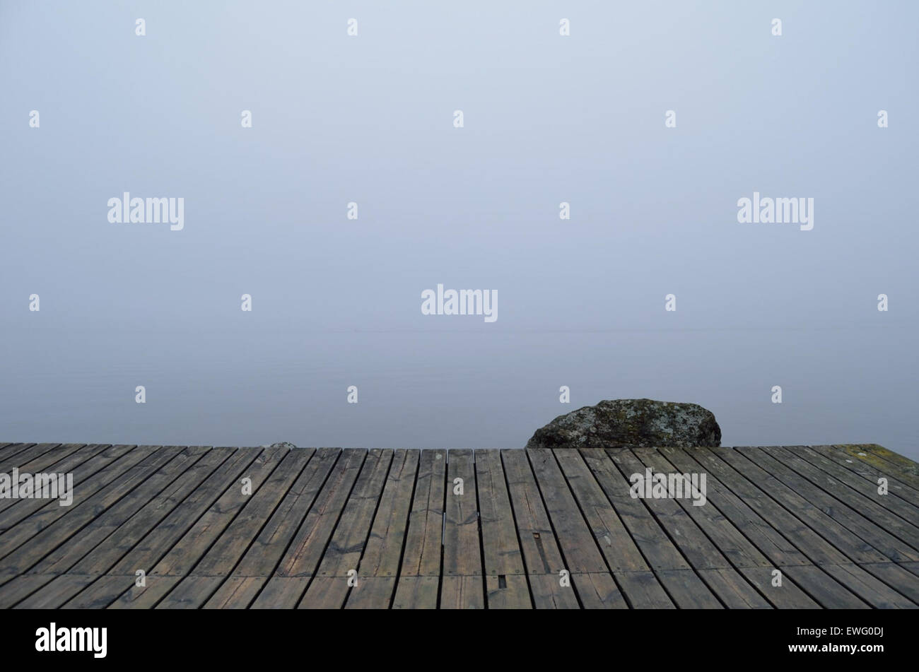 A wooden dock extending over calm water, with rocks visible along the ...