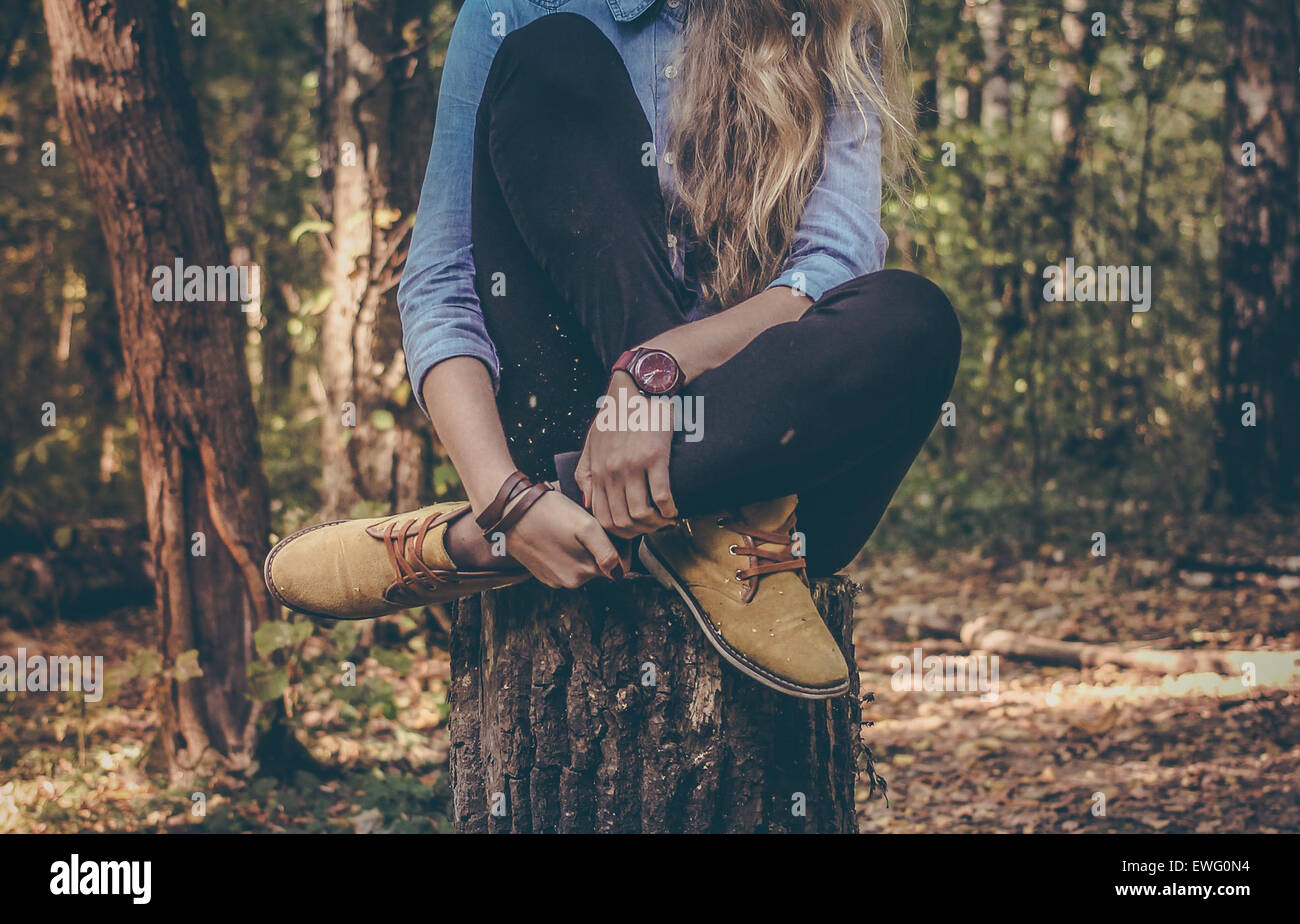 A woman sitting on a tree stump in a forested area, taking a moment to ...