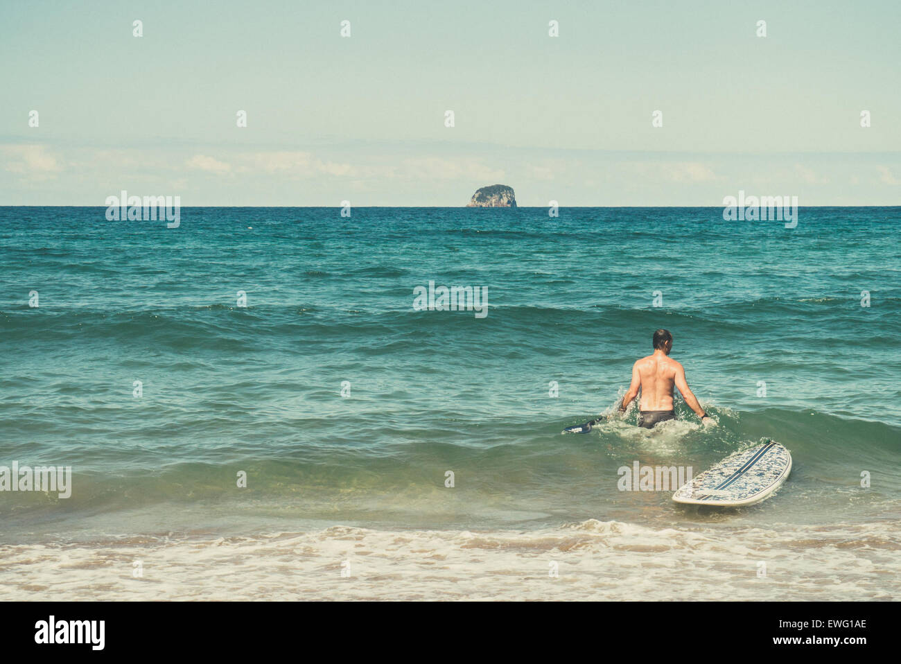 A male surfer rides a wave in the ocean, balancing on his surfboard ...