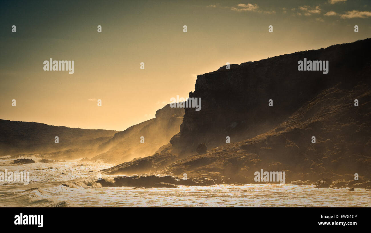 A dramatic ocean cliff scene during sunset, with waves crashing against ...