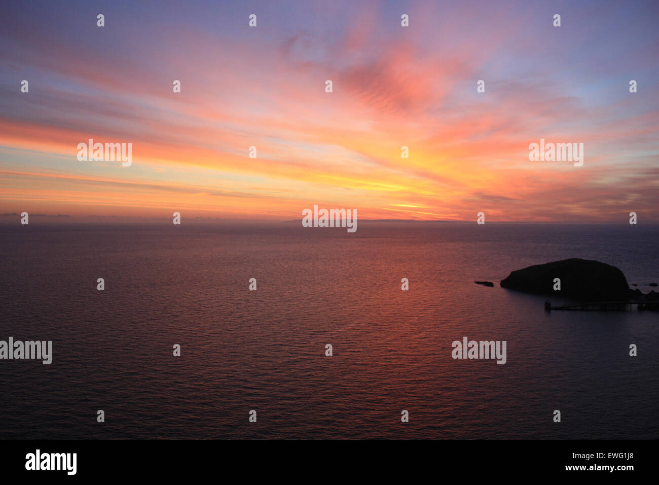 A peach-colored sky at sunset over the ocean, with clouds scattered ...