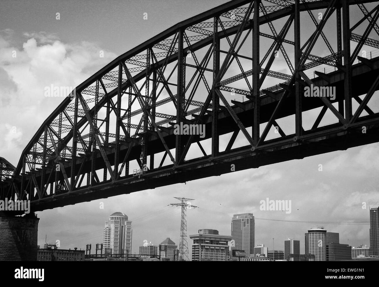 A rail bridge stands alongside power line towers, with a cityscape ...