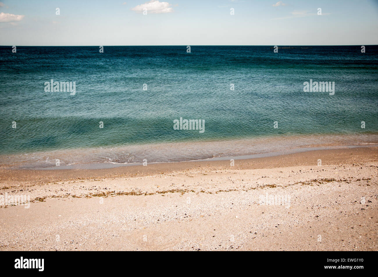 A sandy beach shoreline beside the ocean, where gentle waves meet the ...