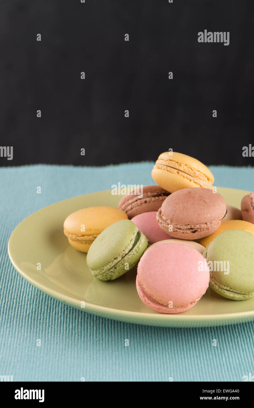 Assortment of gentle colorful macaroons on green ceramic plate on blue ...