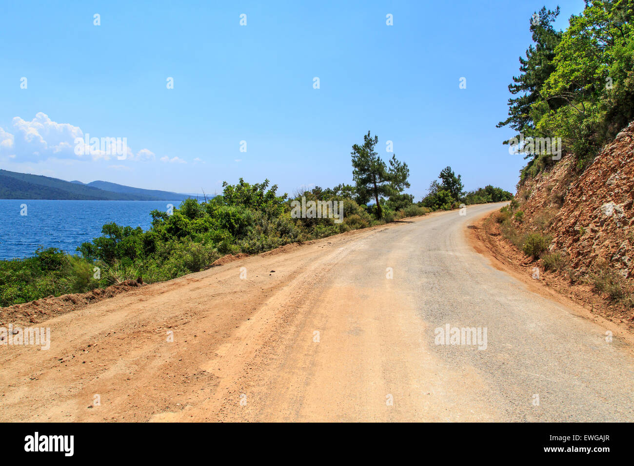 Front view of asphalt road with the view of blue sea and small trees ...