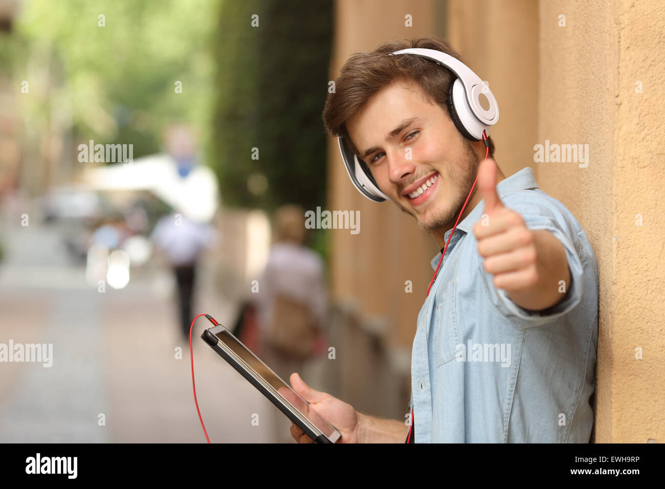 Happy man using a tablet with thumbs up in the street and looking at ...