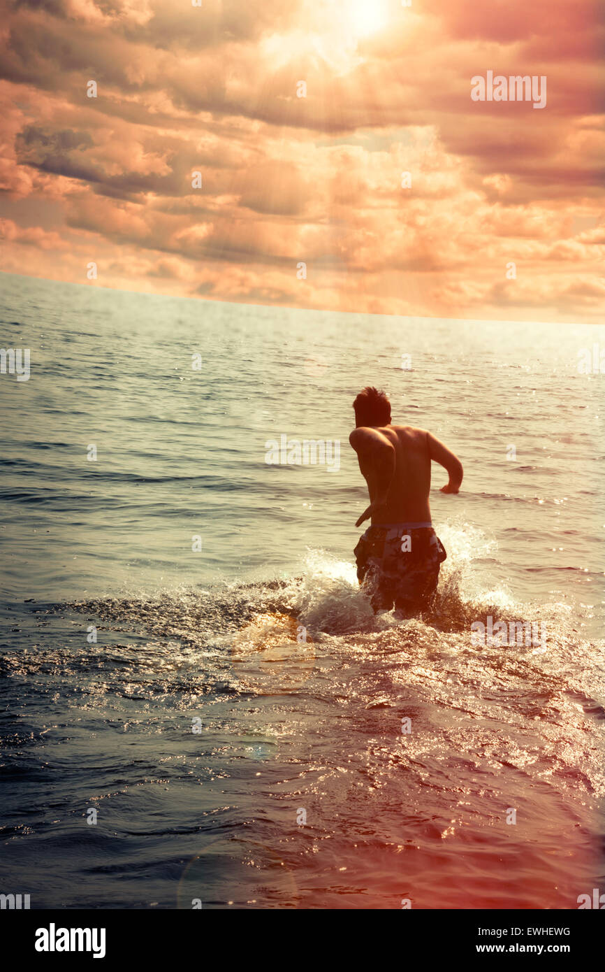 Young man runs out into the sunset lit ocean Stock Photo - Alamy