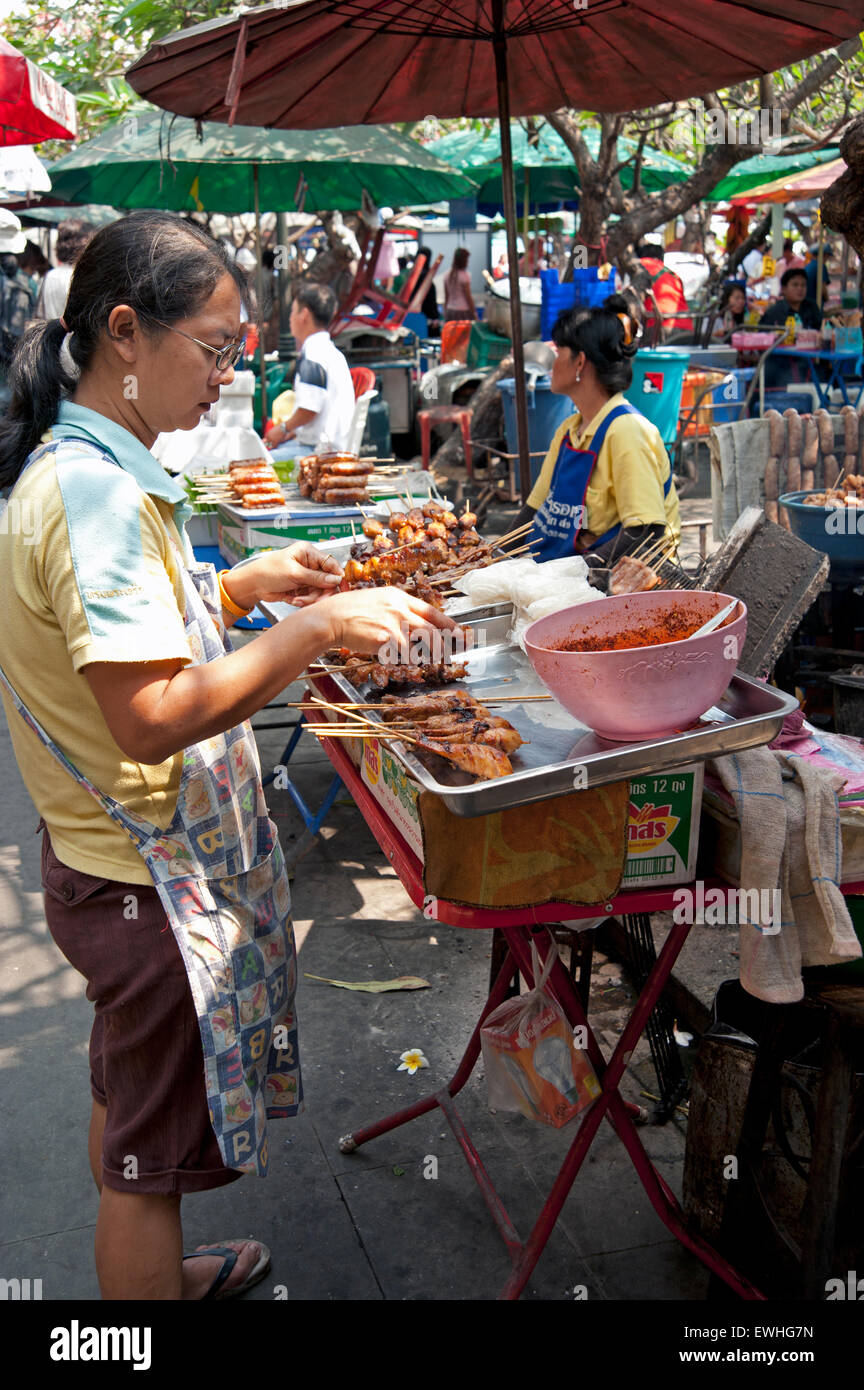 A Thai lady cooking grilled satay sticks in a Bangkok street market ...