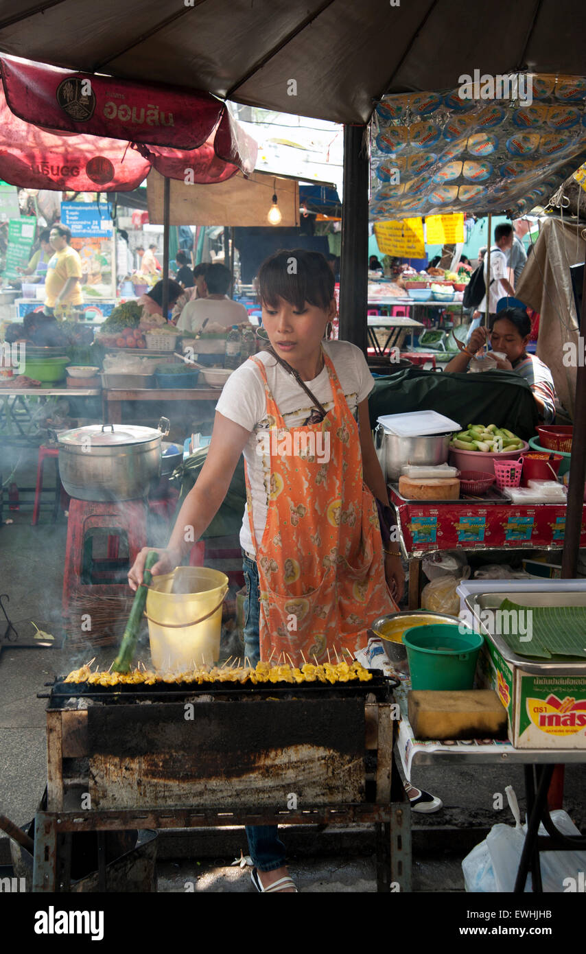 A Thai lady cooking grilled satay sticks in a Bangkok street market ...