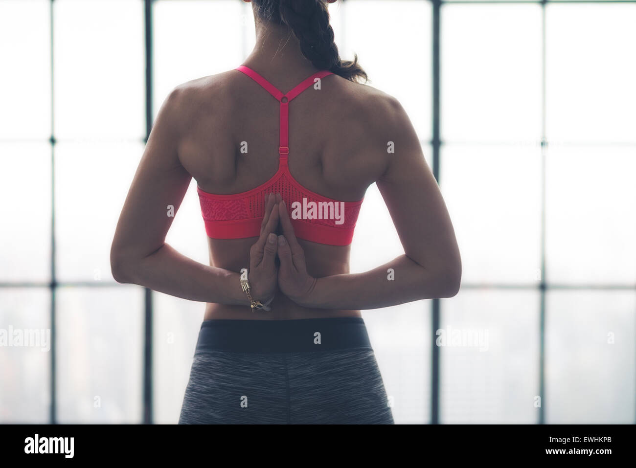A fit, muscular woman's hands clasped behind her back as she is doing ...