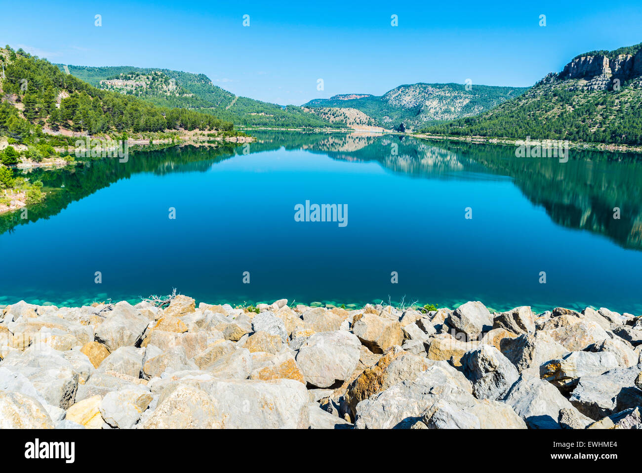 Mountains and vegetation reflected on the calm water of a reservoir in ...