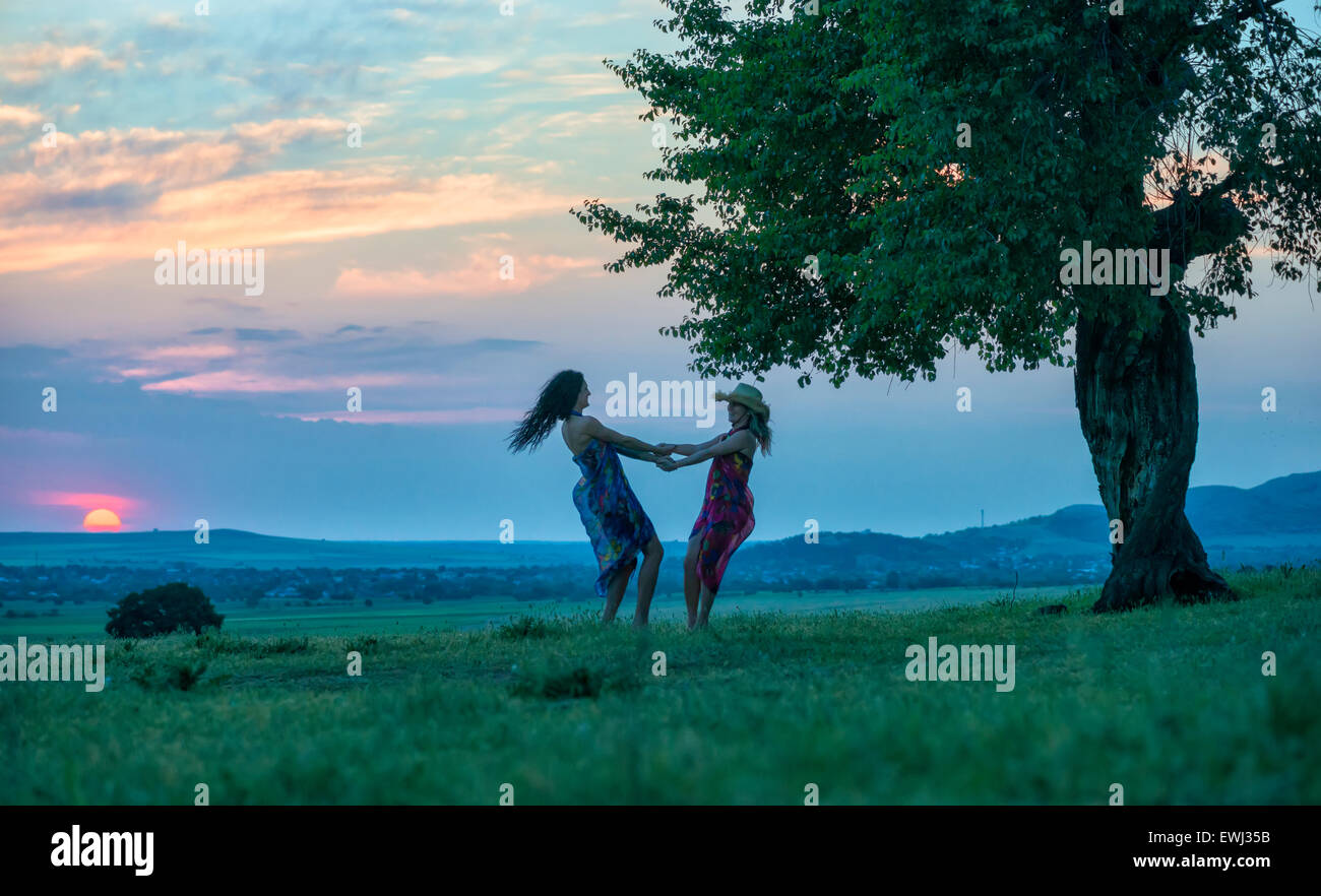 two women dancing on the grass at sunset time Stock Photo - Alamy