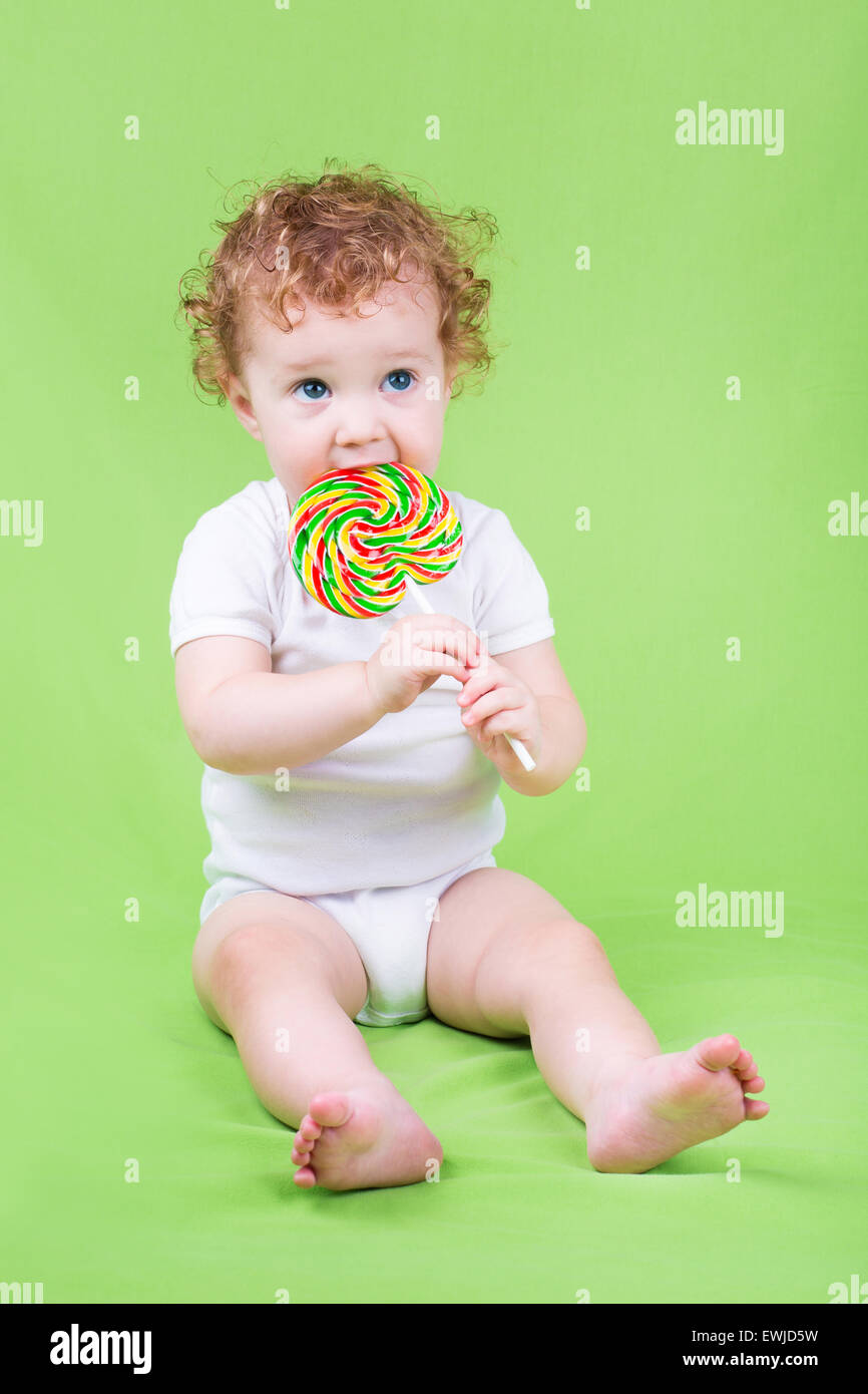 Funny curly baby with a colorful candy on green background Stock Photo ...