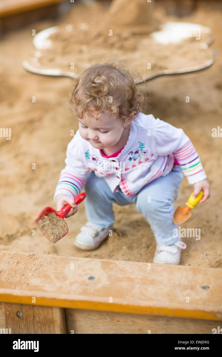 Cute little baby girl digging in sand on a playground Stock Photo - Alamy