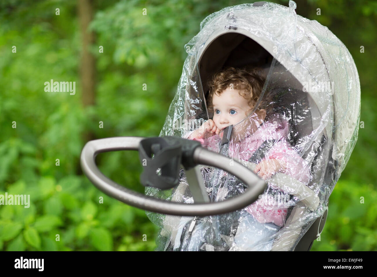 Little baby girl sitting in a stroller under a rain cover on a cold and ...