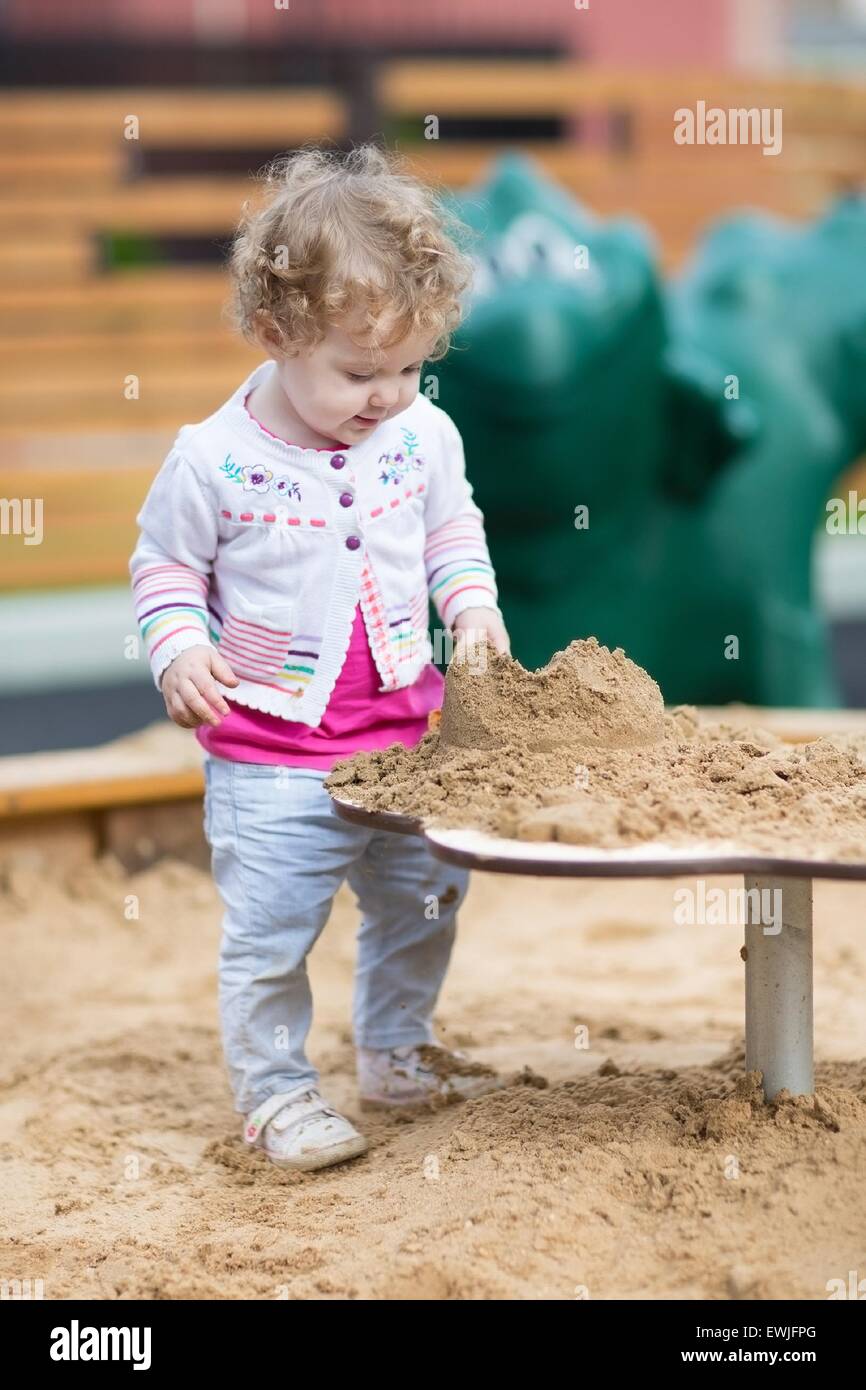 Cute little baby girl digging in sand on a playground Stock Photo - Alamy