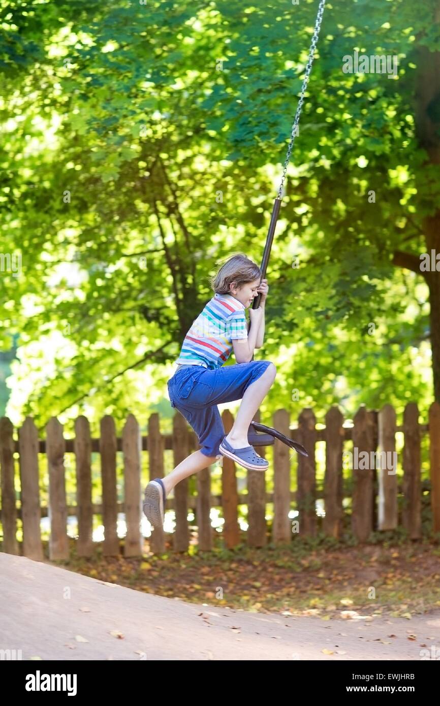 Funny little boy enjoying a swing ride on a playground on a beautiful ...